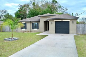 Uma casa residencial com garagem, entrada por um caminho e uma pequena árvore no jardim frontal.