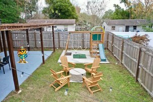 Um quintal com um deck de madeira, balanço, escorrega e uma mesa com cadeiras.