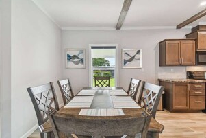 Uma sala de jantar com uma mesa comprida, cadeiras de madeira e vista para uma área externa através de uma porta de vidro.
