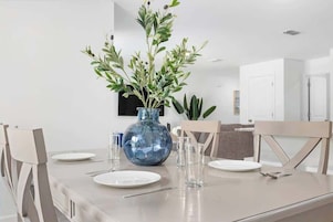 Mesa posta com pratos, talheres e um vaso azul com folhagem verde.