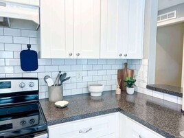 Uma cozinha com armários brancos, fogão, bancada com uma planta e suporte para panelas azul pendurado.
