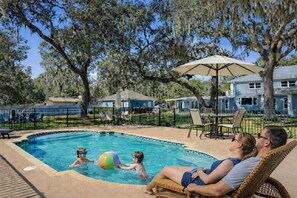 Piscina com uma família e crianças brincando, cercada por um quintal com espreguiçadeiras e guarda-sóis.