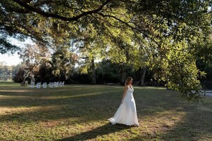Cerimônia de casamento em um parque, com uma noiva em vestido branco, árvores e cadeiras dispostas para os convidados.