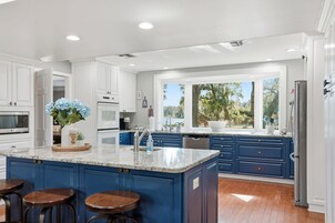 Cozinha moderna com armários brancos, ilha azul e uma grande janela com vista para o exterior.
