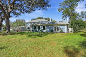 Uma casa de dois andares com um amplo jardim frontal, varanda coberta e garagem visível.