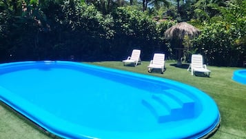 Piscina com três espreguiçadeiras e uma cobertura de palha.