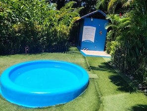 Piscina inflável azul cercada por vegetação exuberante e um pequeno galpão azul com uma placa.