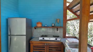 Uma cozinha compacta com geladeira, fogão a gás e uma pequena prateleira com uma panela e uma chaleira.