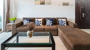 Uma sala de estar com um sofá seccional marrom, uma mesa de centro de vidro e almofadas decorativas.