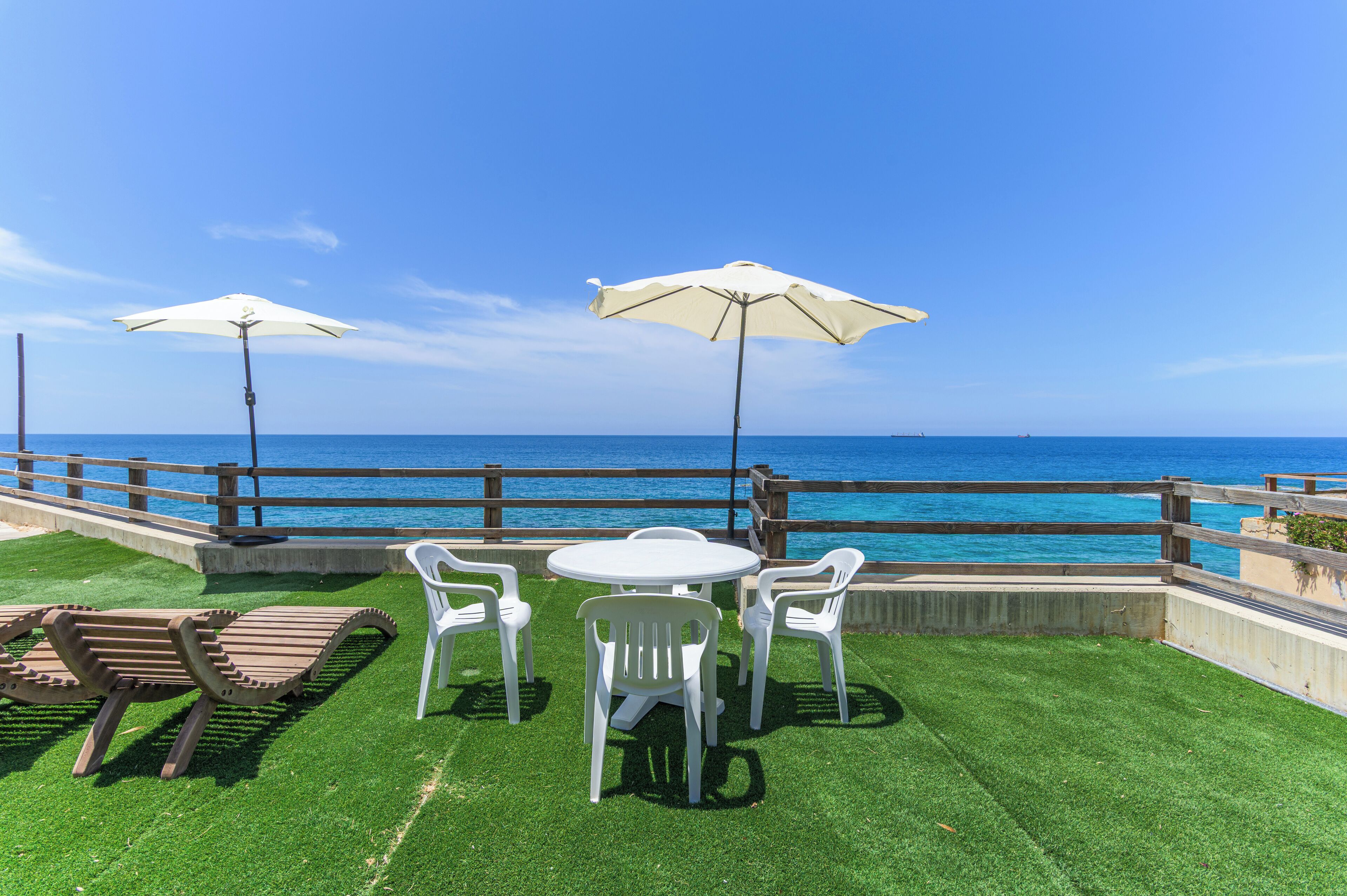 Pátio com vista para o oceano, com uma mesa, cadeiras, dois guarda-sóis e uma poltrona de madeira.