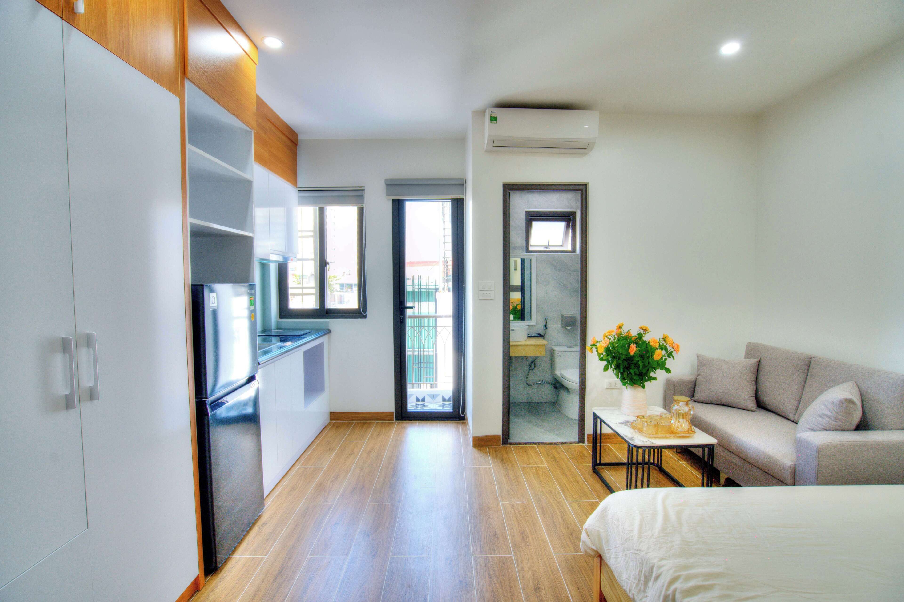 Um espaço de estar moderno e compacto com cozinha compacta, um sofá e uma pequena mesa com um vaso de flores.