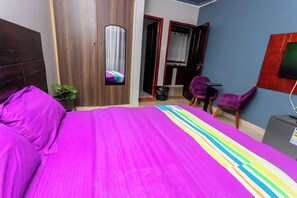 Quarto com uma cama grande, guarda-roupa, espelho, mesa pequena, cadeira e televisão.
