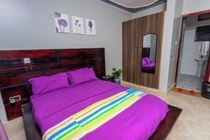 Quarto com cama, cabeceira de madeira, guarda-roupa, espelho e mesa de cabeceira.
