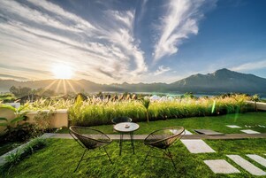 Um pátio com duas cadeiras e uma mesa, com vista para uma paisagem deslumbrante de um lago e montanhas.