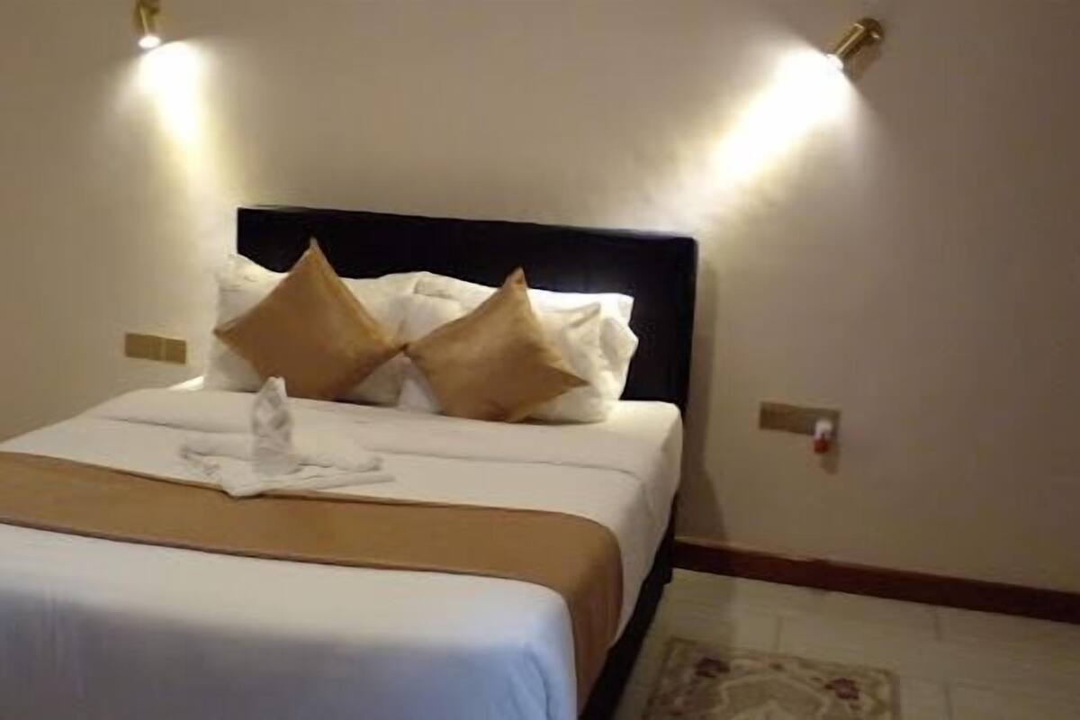Uma cama bem arrumada com um edredom branco e bege, duas almofadas douradas e uma toalha branca.