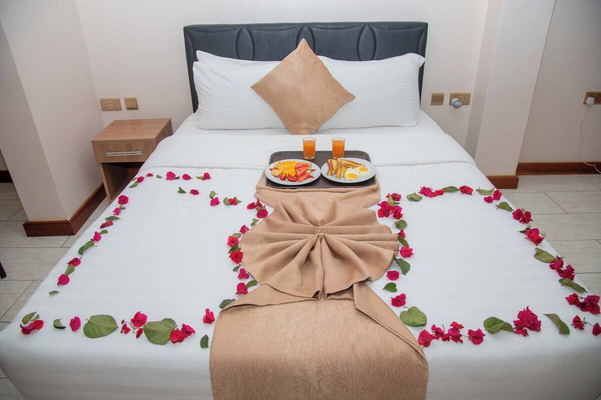 Cama bem arrumada com bandeja de café da manhã, travesseiros e um arranjo floral decorativo.