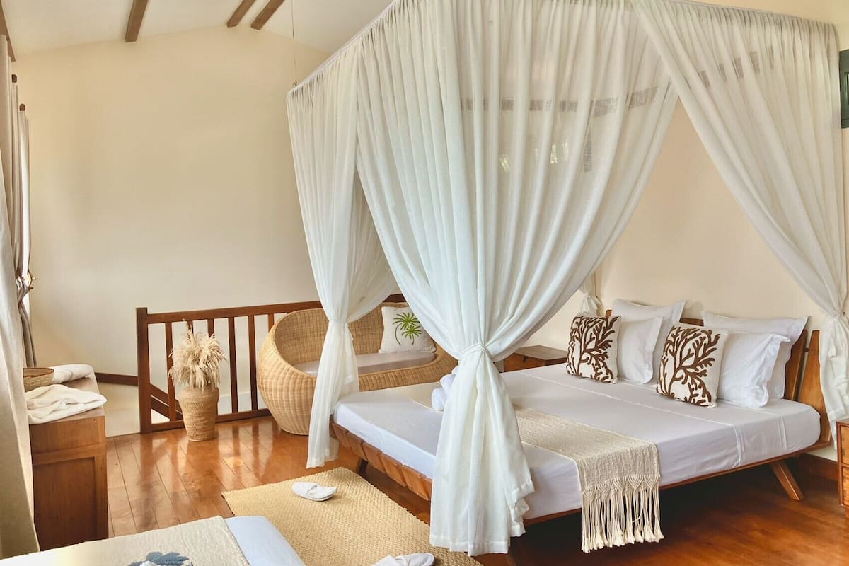 Quarto com cama de dossel, piso de madeira e ventoinha no teto.