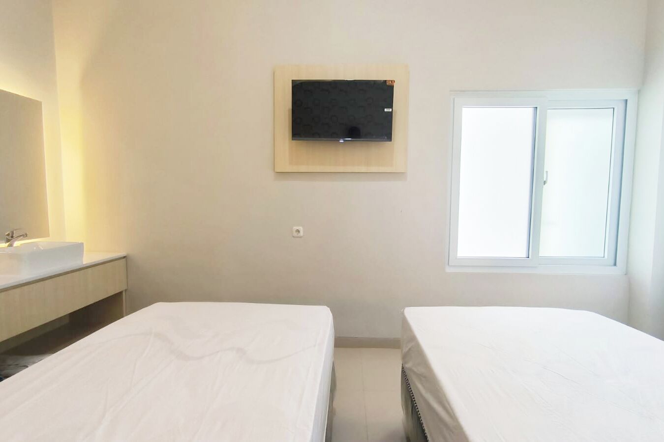 Quarto de hotel com duas camas, um espelho grande, televisão na parede e janela com luz natural.