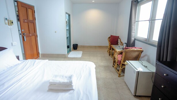 Quarto de hotel com cama, uma mesa pequena, uma cadeira, um refrigerador e uma janela com cortinas.