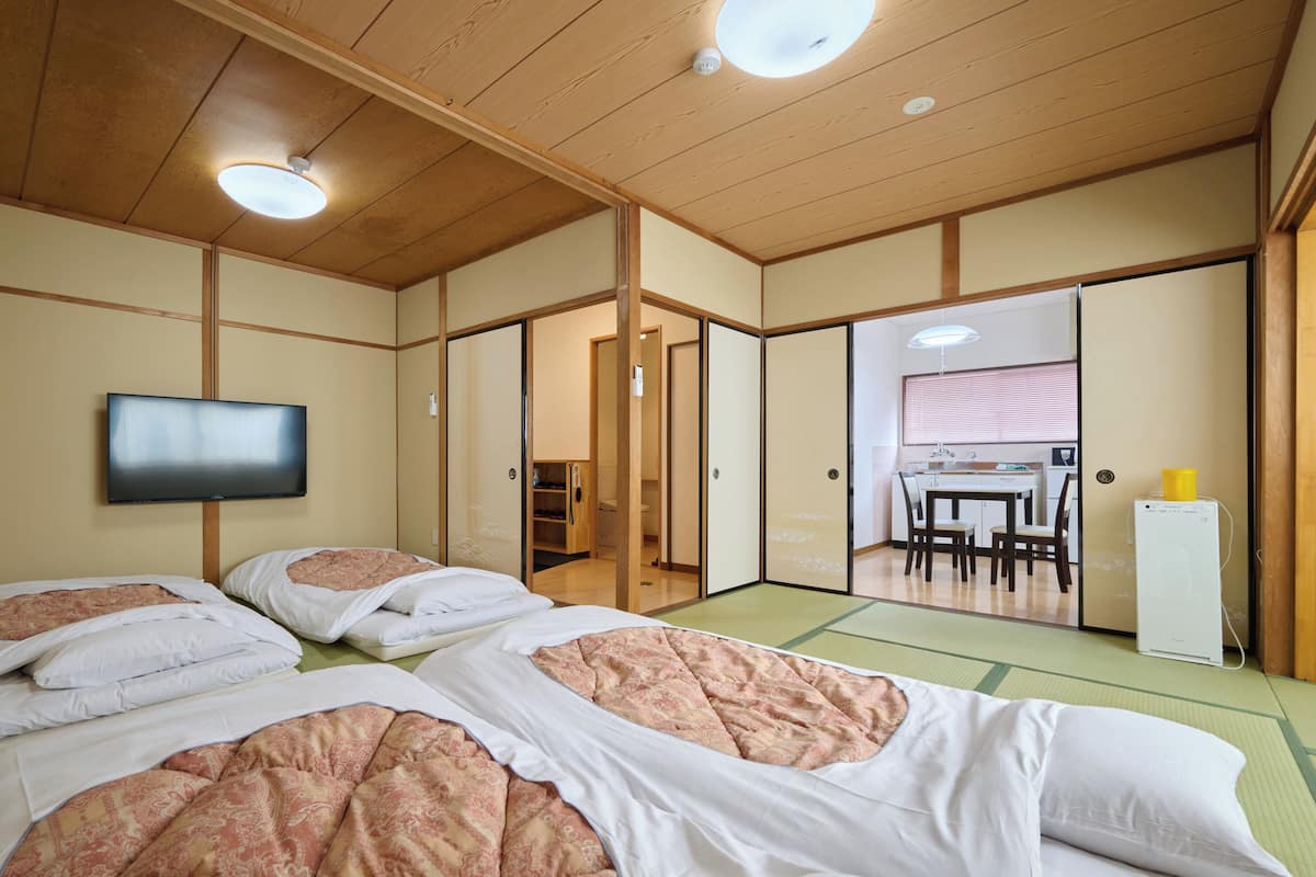 Quarto de hotel com duas camas, televisão, área de refeições e cozinha.