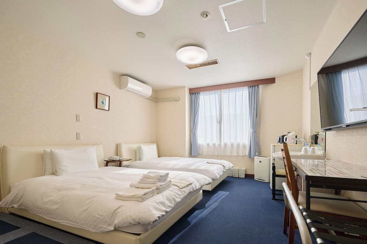 Quarto de hotel com duas camas, uma escrivaninha, uma cadeira, uma TV e uma janela com cortinas.