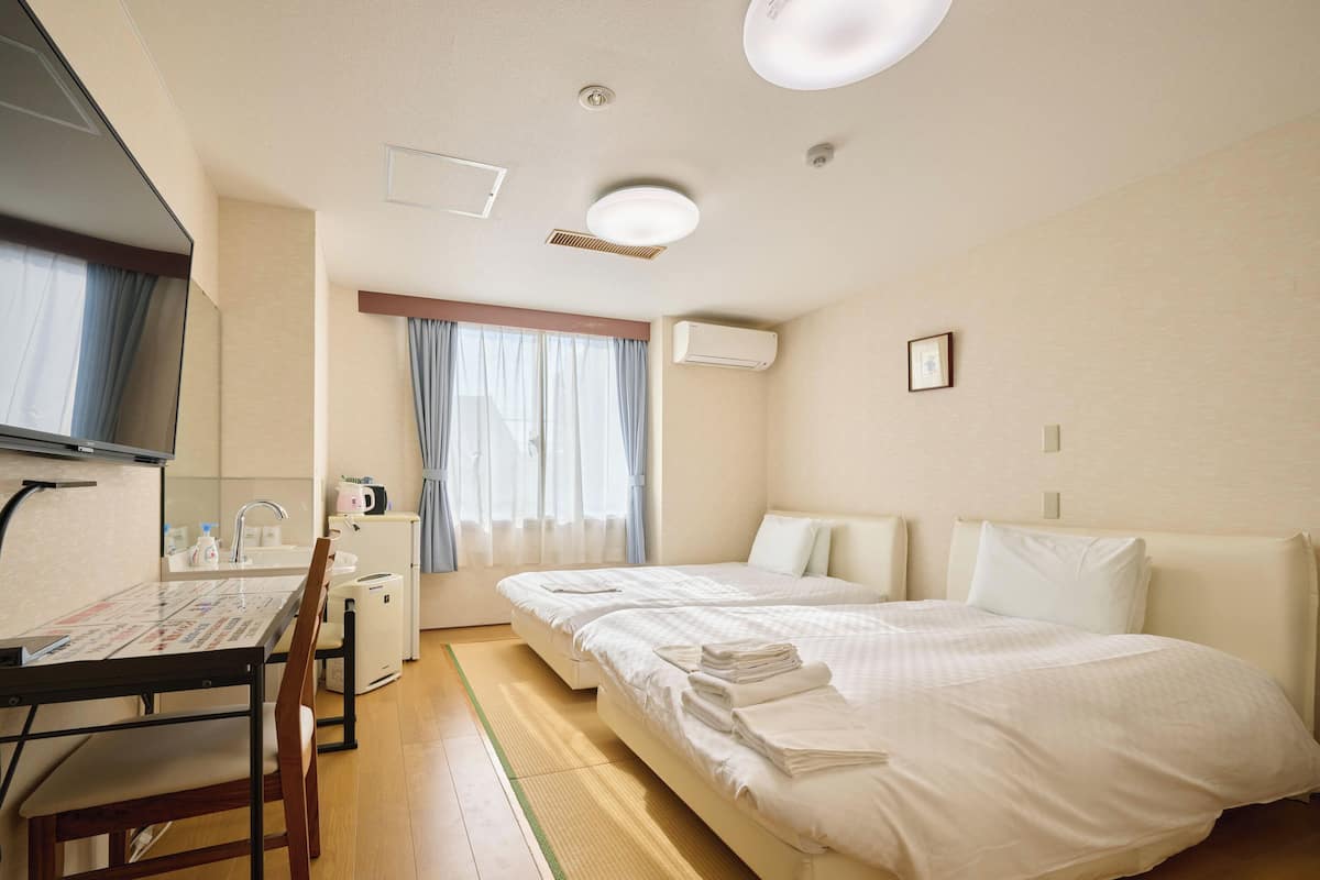 Quarto de hotel com cama, secretária com cadeira, televisão, janela com cortinas e ar condicionado.
