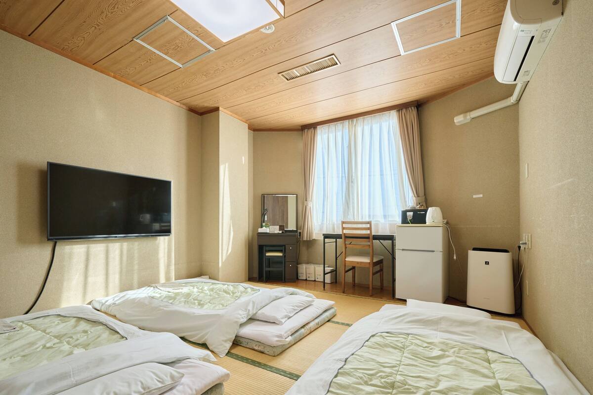Quarto de hotel com duas camas, uma escrivaninha, uma cadeira, uma televisão e um pequeno frigorífico.