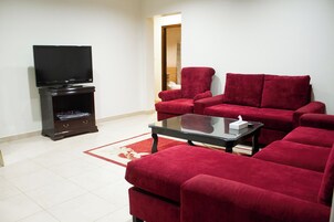 Sala de estar com televisão de tela plana, móvel para home theater em madeira escura, sofás de veludo vermelho e mesa de centro de vidro.
