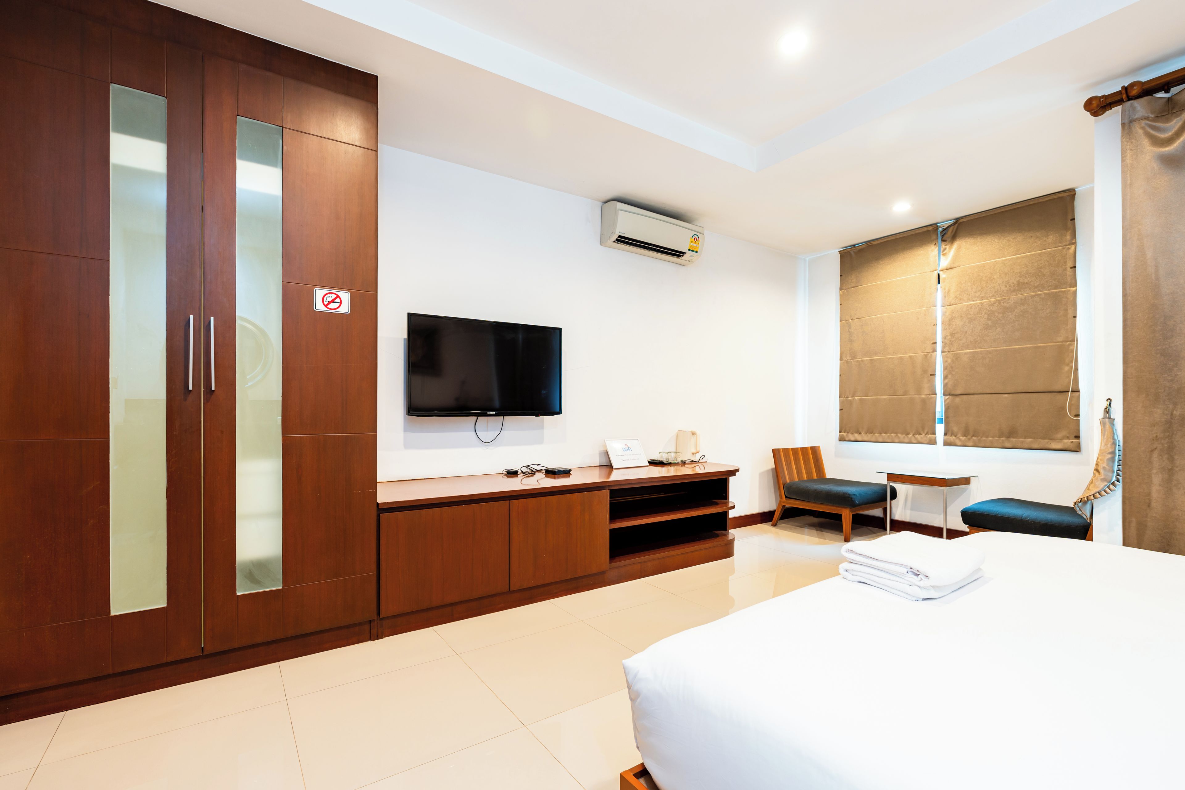 Quarto de hotel com cama, televisão, secretária, cadeira e guarda-roupa.