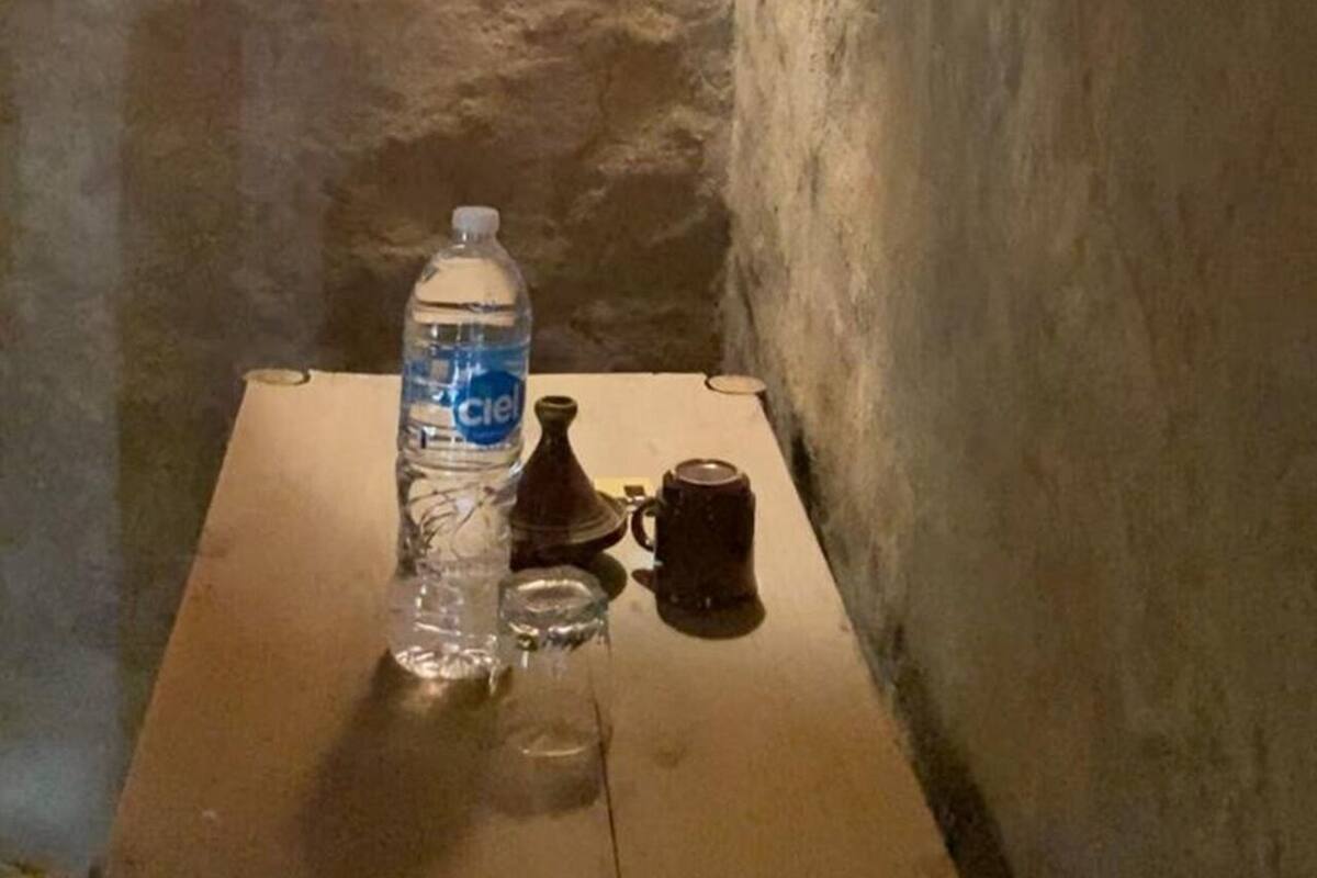 Canto com parede texturizada, uma mesa pequena com uma garrafa de água, um copo e uma caneca.