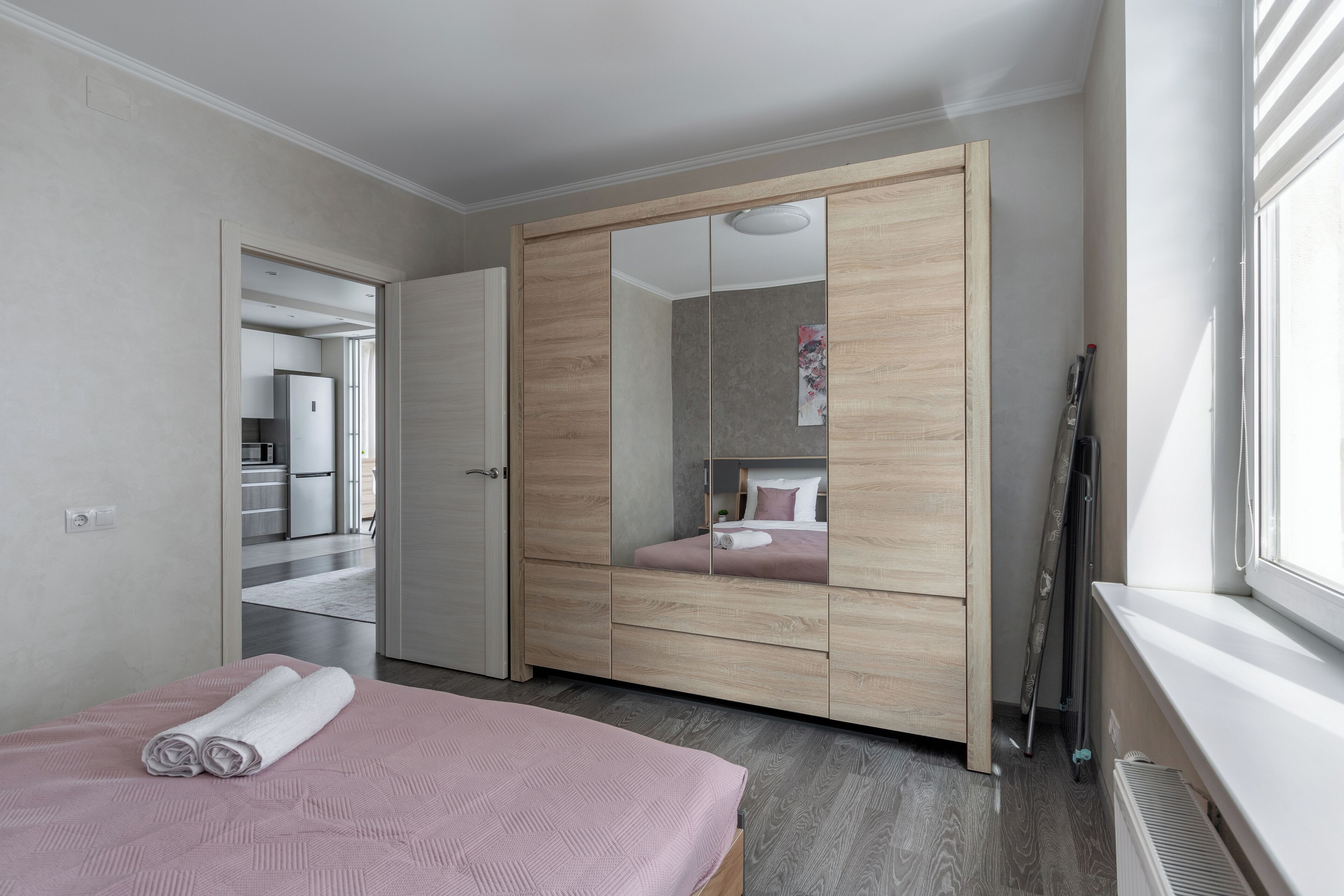 Quarto com cama, guarda-roupa, espelho e janela.