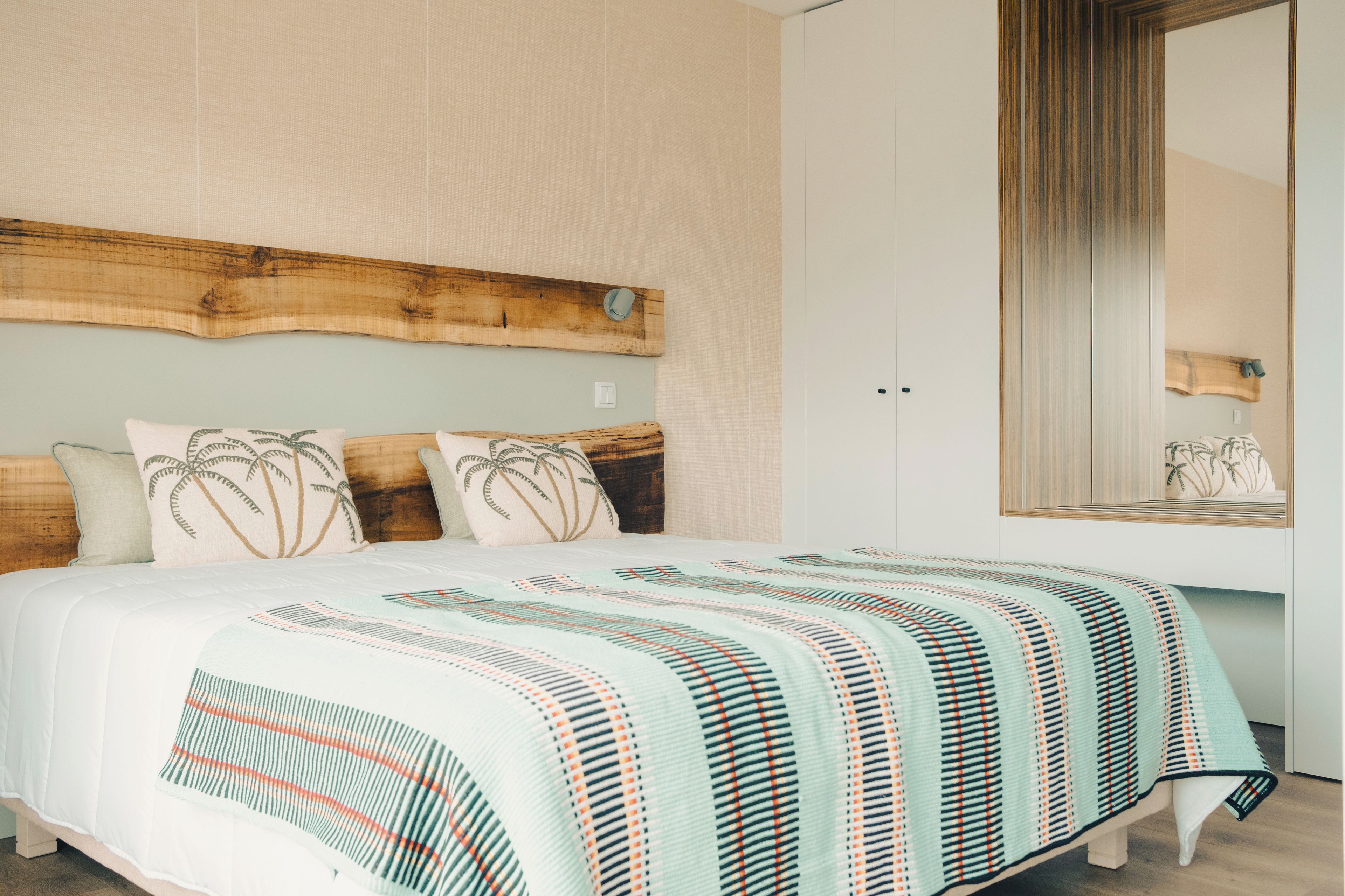 Quarto com cama, cabeceira de madeira, um espelho grande e um guarda-roupa.
