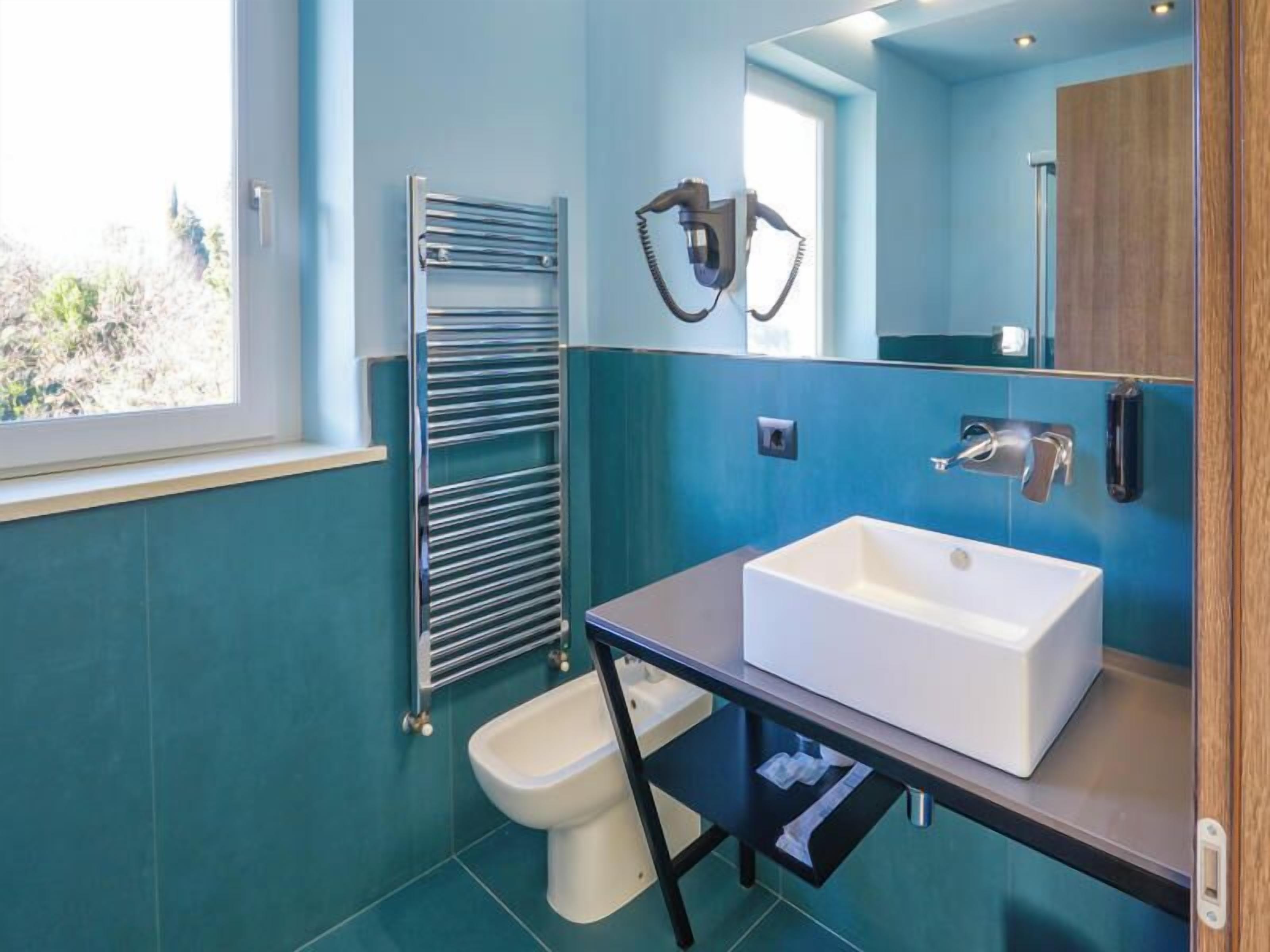Uma casa de banho moderna com uma janela ampla, uma pia branca, um bidé e um porta-toalhas.