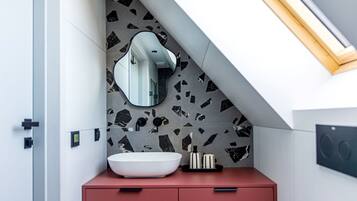Uma casa de banho moderna com uma pia branca, toucador vermelho e um mosaico preto e cinzento peculiar no painel de fundo.