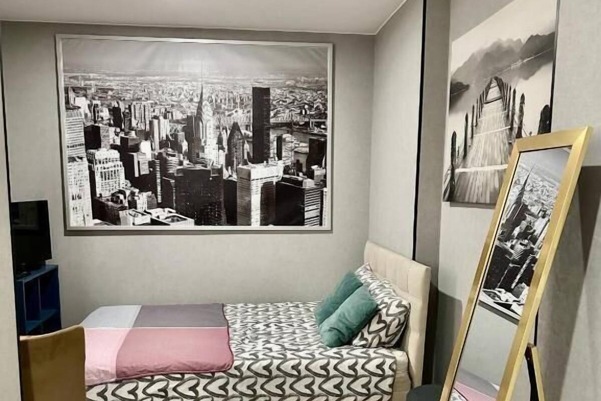 Quarto com cama, pintura de paisagem urbana, espelho e tapete.