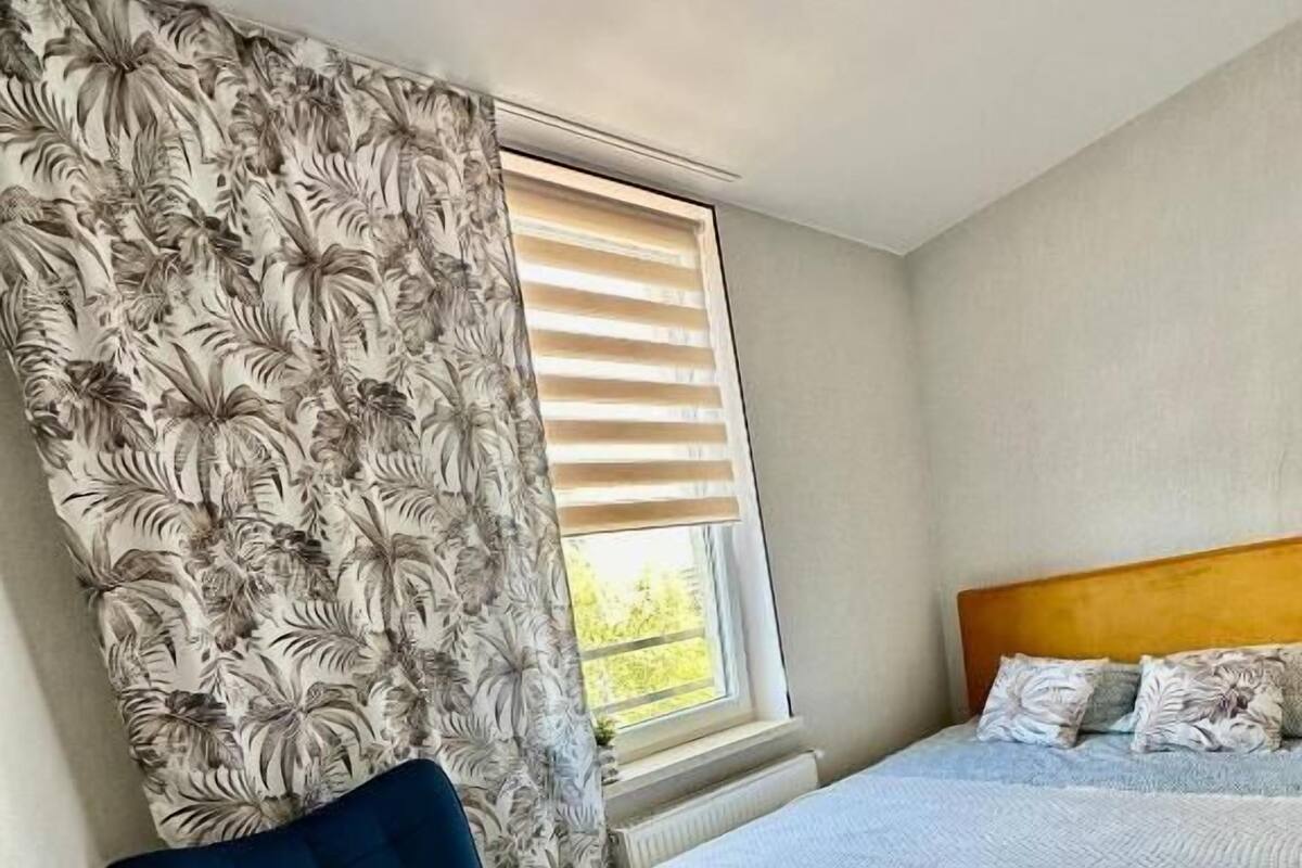 Um quarto com uma cama, uma cadeira azul, um banco e uma janela com persianas.