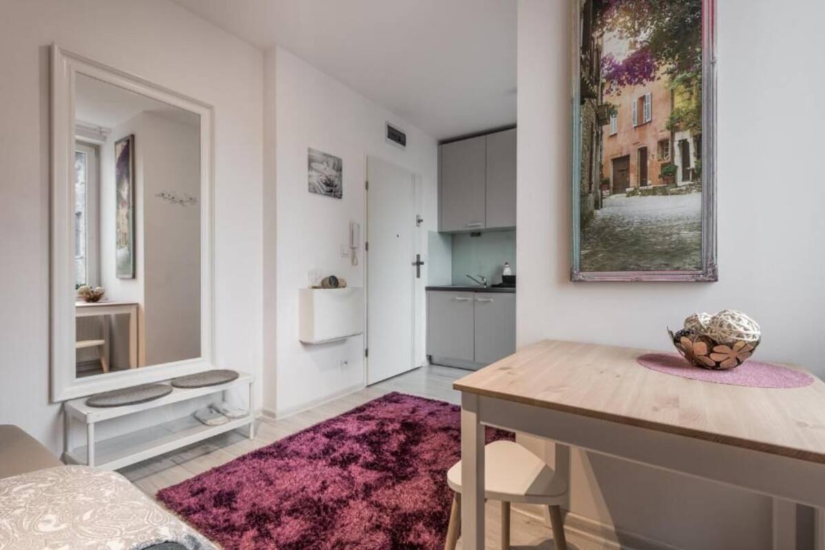 Quarto moderno e bem iluminado, com um espelho grande, uma mesa de madeira e um tapete roxo.