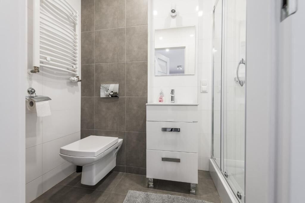 Uma casa de banho moderna com sanita, cabine de duche em vidro e toucador branco com espelho.