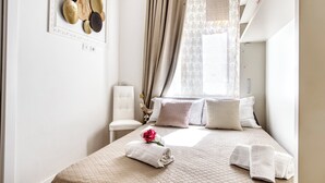 Quarto bem arrumado com uma cama, almofadas, uma cadeira e uma janela com cortinas.