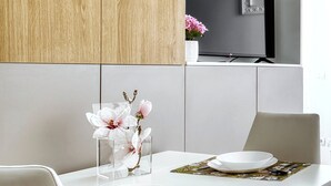 Uma cozinha moderna com armários brancos, uma TV de tela plana e uma mesa de jantar posta com pratos e um vaso de flores.