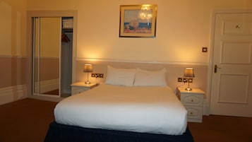 Quarto de hotel com cama, duas mesas de cabeceira com abajures, uma porta, um espelho e um quadro na parede.