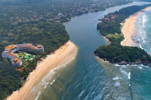 Vista aérea de uma área costeira com um hotel de design curvo, uma praia e um rio.
