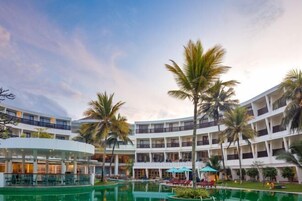 Um hotel com vários andares, um pátio central com piscina e palmeiras.