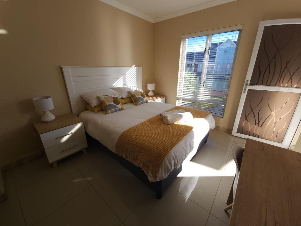 Quarto com cama grande, mesas de cabeceira, janela com persianas e obra de arte na parede.