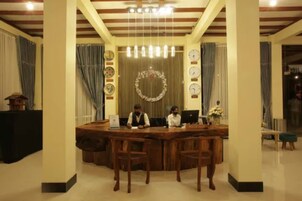 Uma receção com dois funcionários, um balcão de madeira e um candelabro.