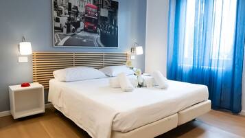 Uma cama bem arrumada com lençóis brancos, uma cabeceira com ripas horizontais, uma mesa de cabeceira com um objeto vermelho, um quadro na parede de um ônibus vermelho e uma janela com cortinas azuis.