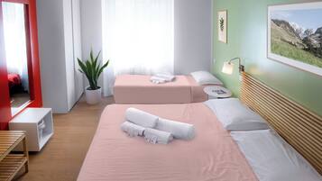 Quarto de hotel com uma cama grande, um sofá pequeno, uma planta em vaso, uma janela com cortinas leves e um quadro na parede.
