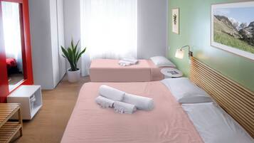 Quarto de hotel com uma cama grande, um sofá pequeno, uma planta em vaso, uma janela com cortinas leves e um quadro na parede.