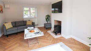 Uma sala de estar moderna com um sofá cinzento, uma mesa de centro com livros e um prato de comida, uma lareira e uma TV fixada na parede.