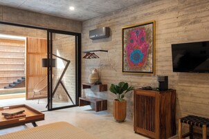 Uma sala de estar moderna com piso de madeira, uma janela grande, um sofá, uma mesa de centro, uma TV montada na parede e uma escada que leva a uma área externa.